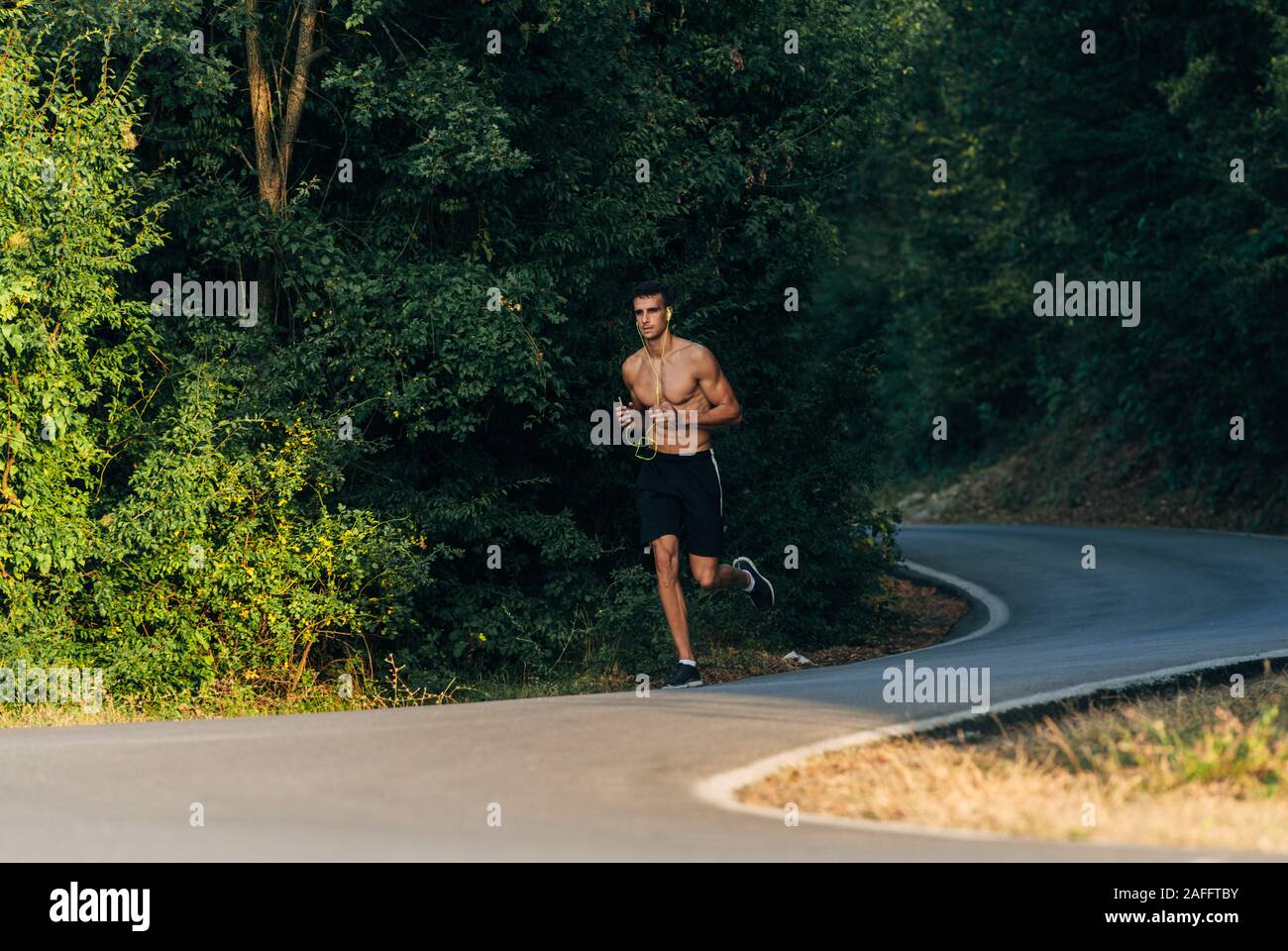 Shirtless male runner with headphones. Man running into sunset on ...