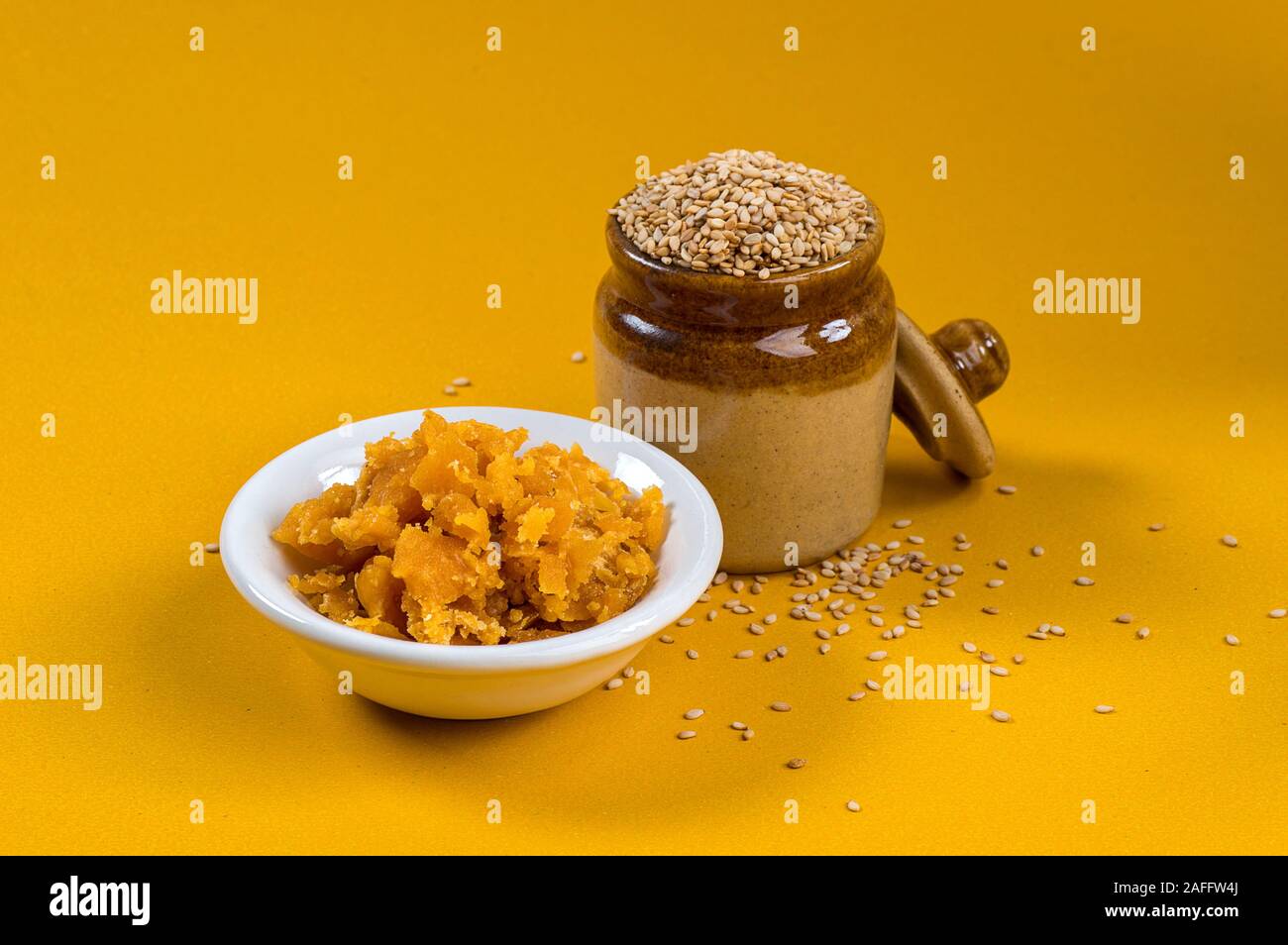 Sesame Seeds in clay pot with Jaggery in bowl on yellow background ...