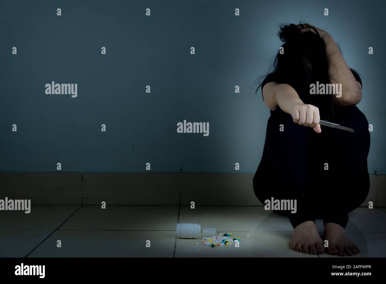 sad woman hug her knee and cry sitting alone and holding a cutter knife ...