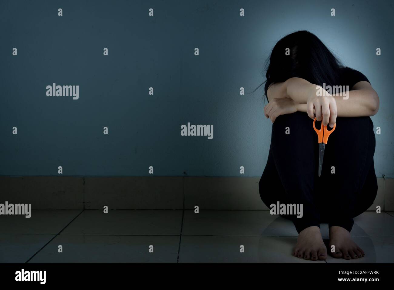 sad woman cry sitting alone and holding a scissors in a dark room ...