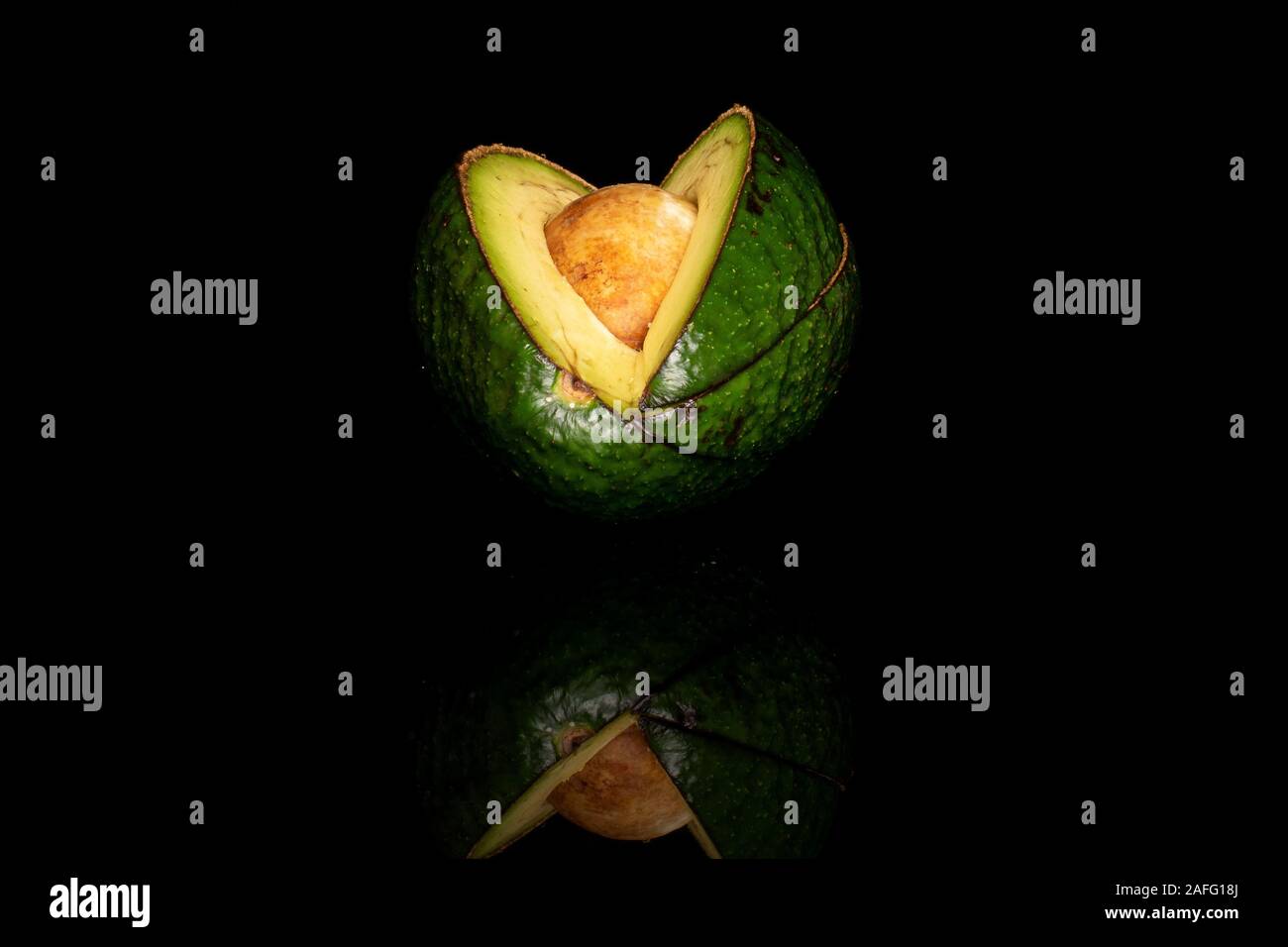 One whole fresh green avocado with cut quarter isolated on black glass ...