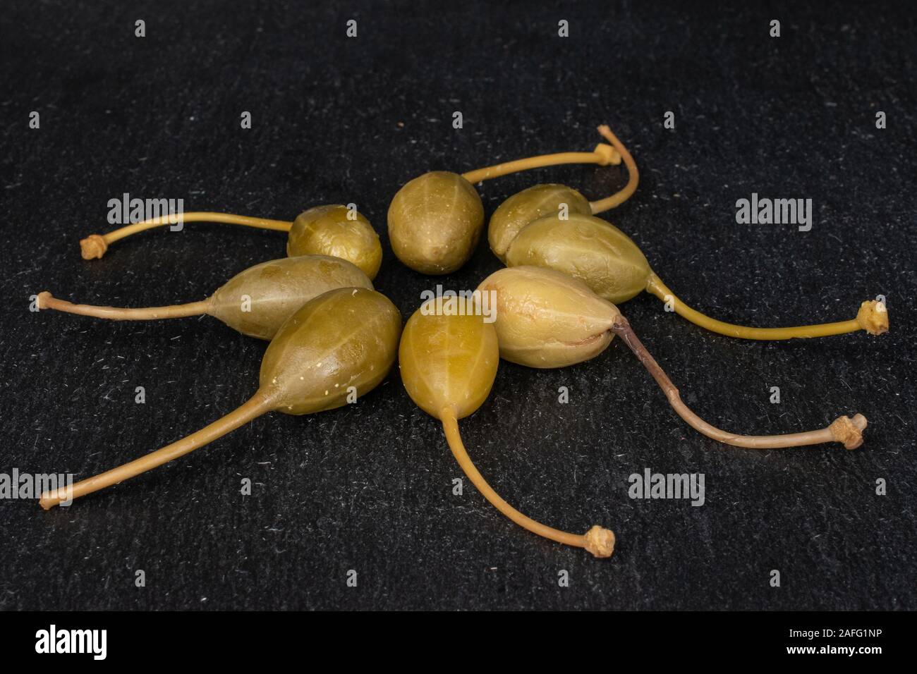 Group of eight whole pickled green caper on grey stone Stock Photo - Alamy