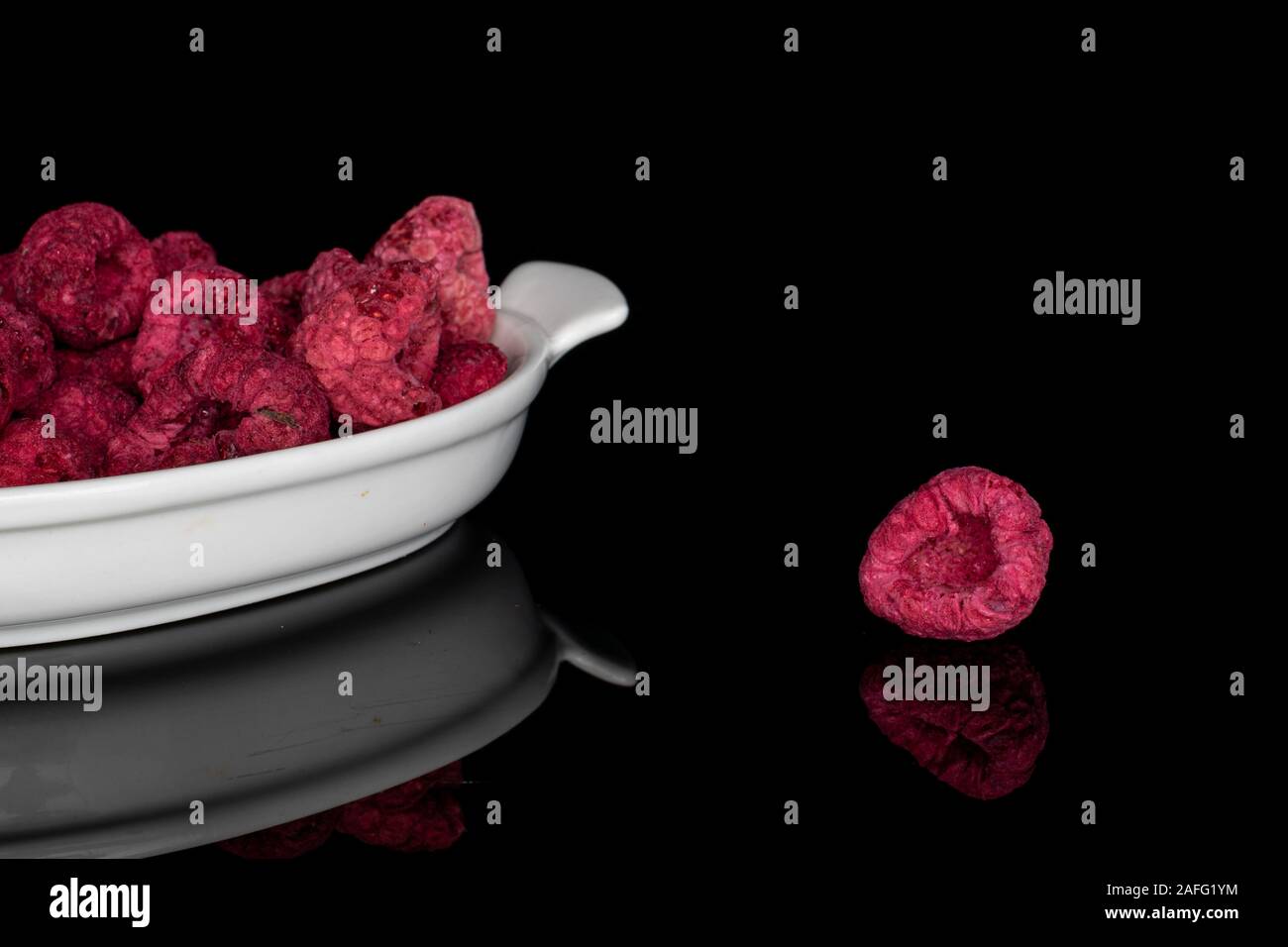 Lot of whole dried raspberry on white ceramic plate isolated on black ...