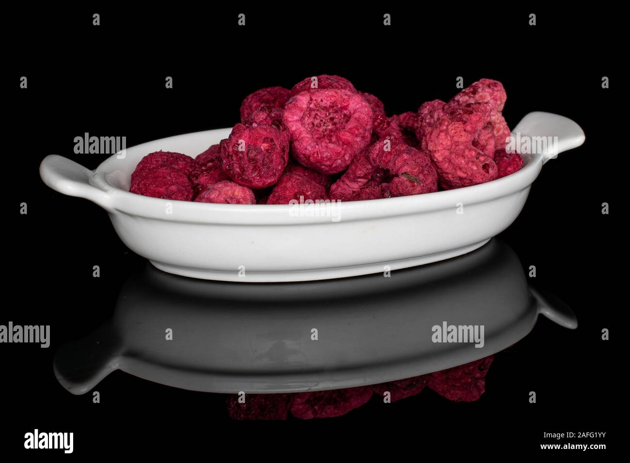Lot of whole dried raspberry on white ceramic plate isolated on black ...