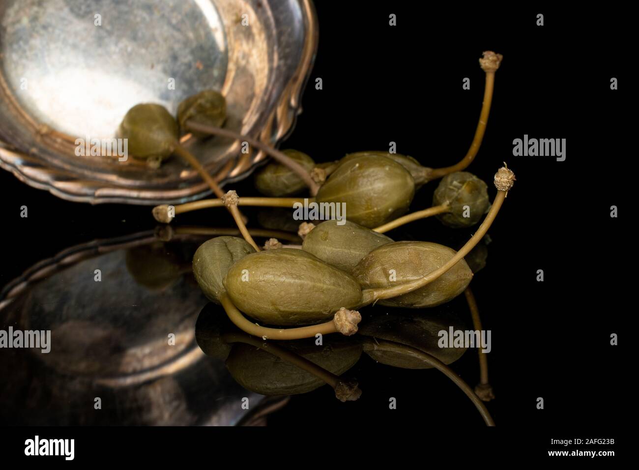 Lot of whole pickled green caper in copper bowl isolated on black glass ...