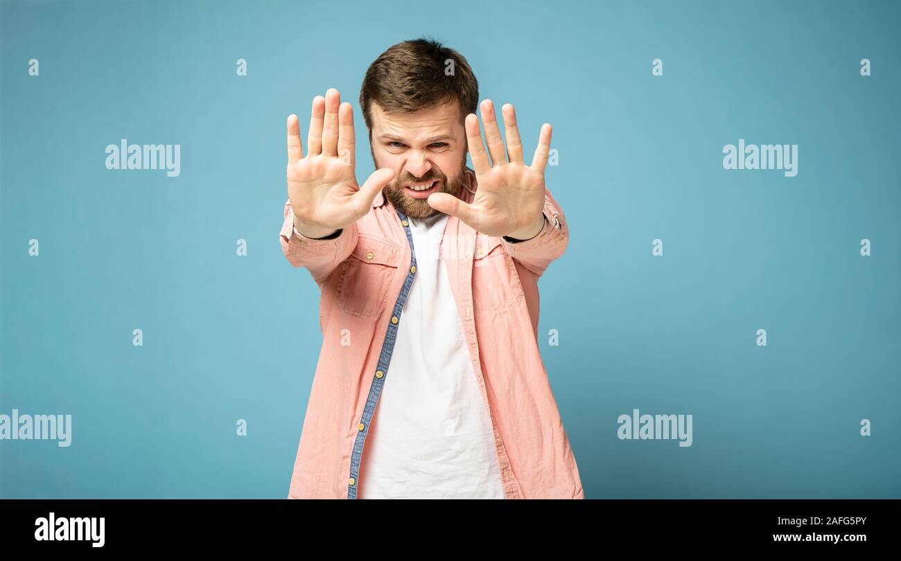 Bearded man confidently extended palms as protection, squinted, and ...