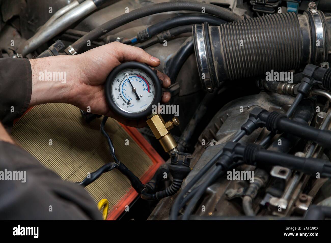 A male mechanic measures the compression in the cylinder of a car ...
