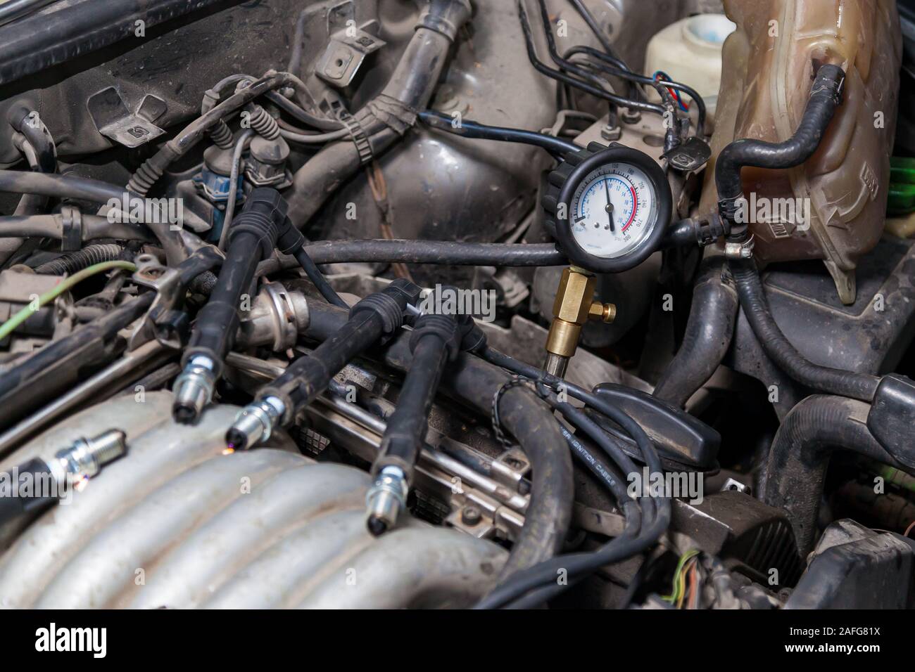 A male mechanic measures the compression in the cylinder of a car ...