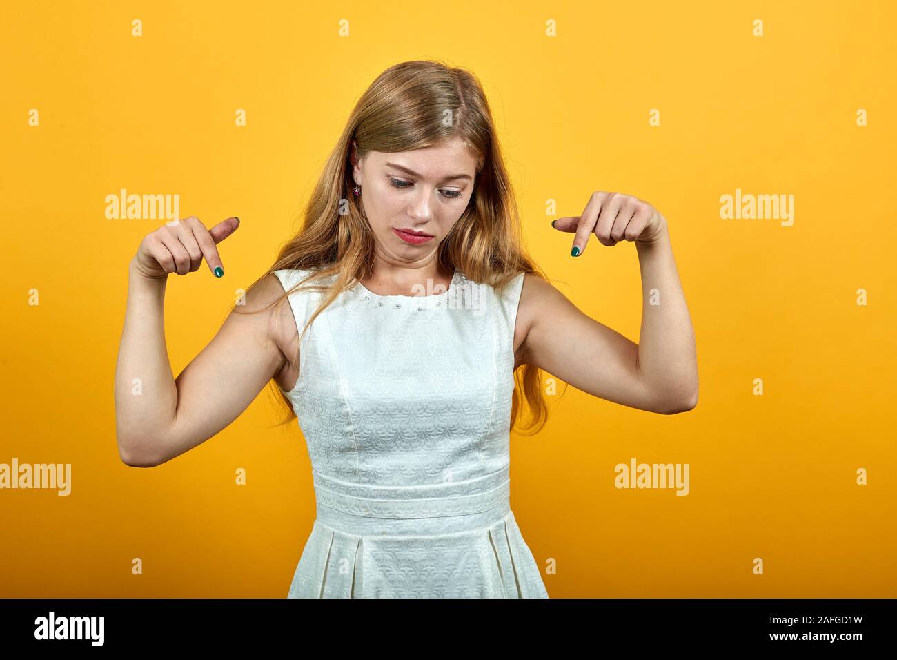 Disappointed young charming woman pointing fingers down, looking sad ...