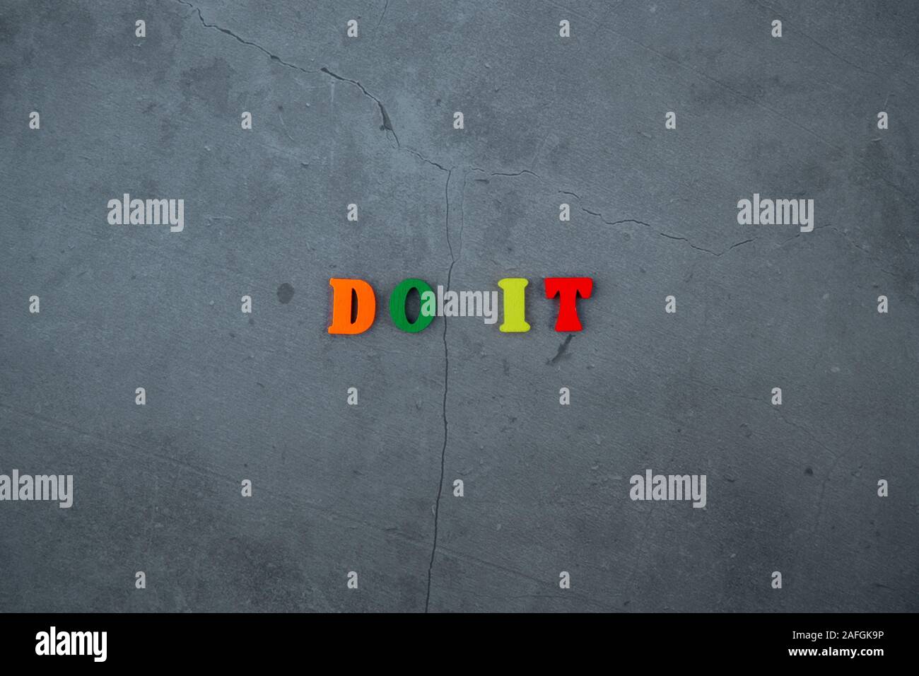 The multicolored do it word is made of wooden letters on a grey ...