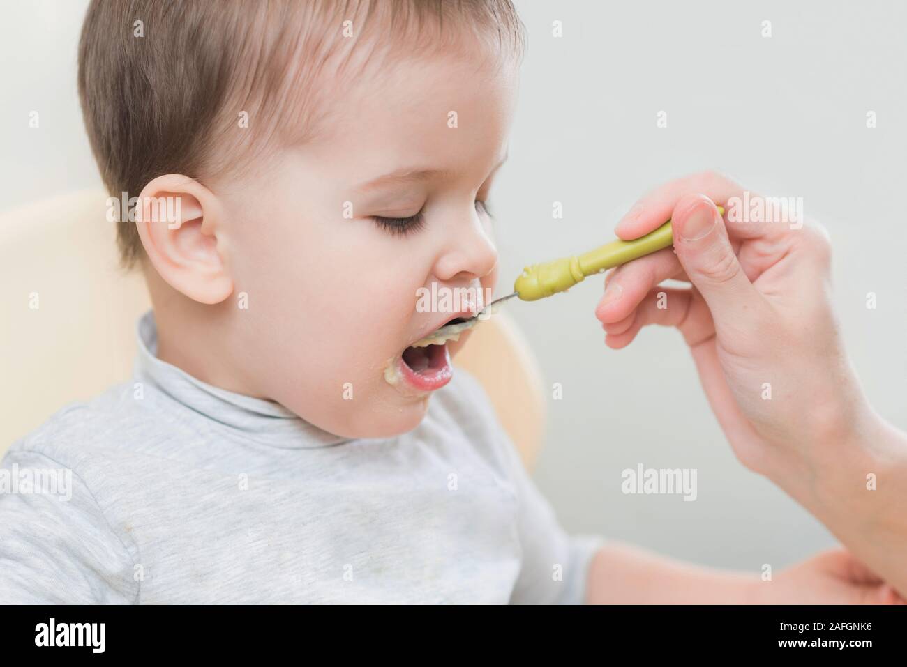 mom in the kitchen is feeding the baby porridge Stock Photo - Alamy