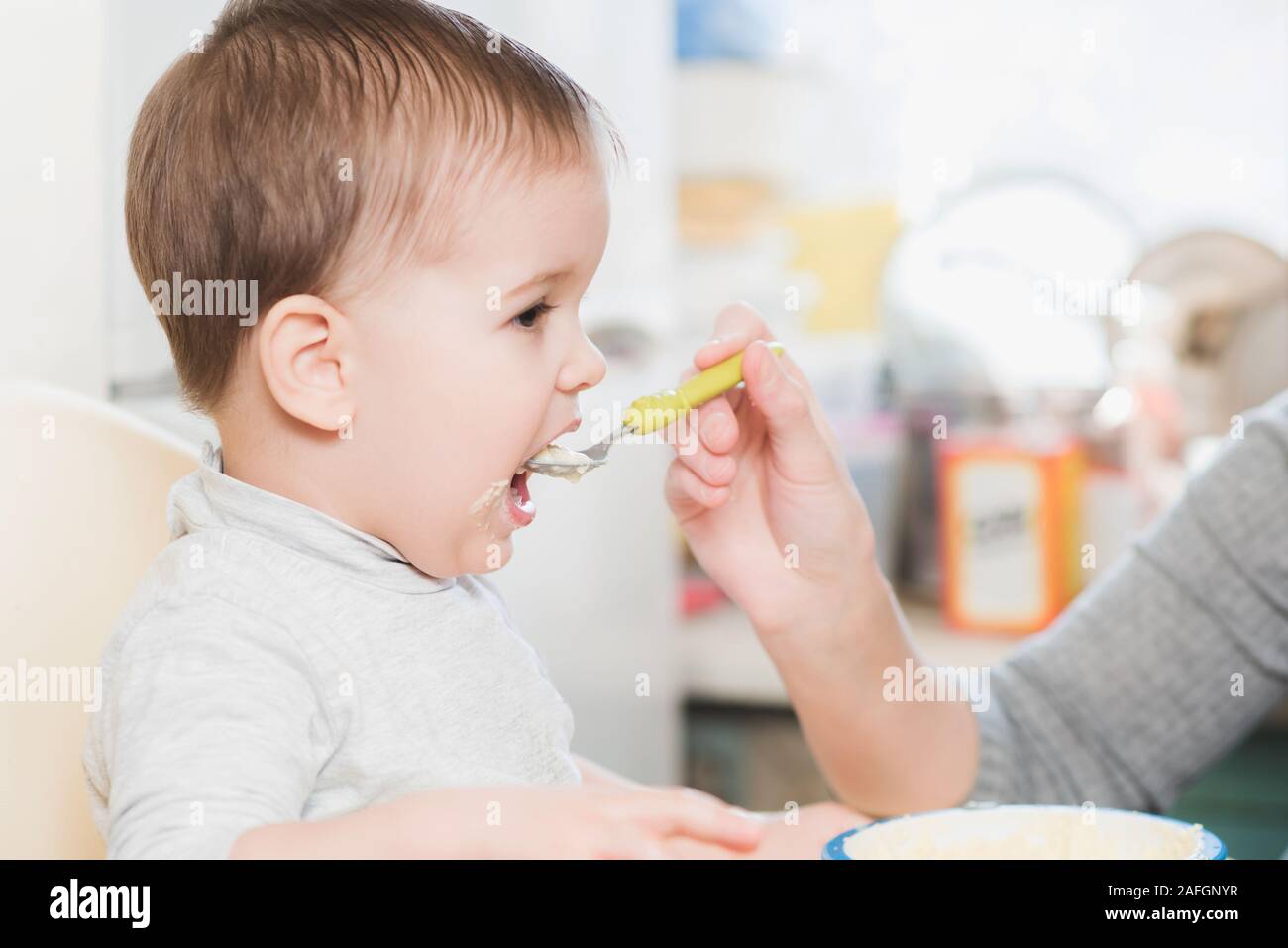 mom in the kitchen is feeding the baby porridge Stock Photo - Alamy
