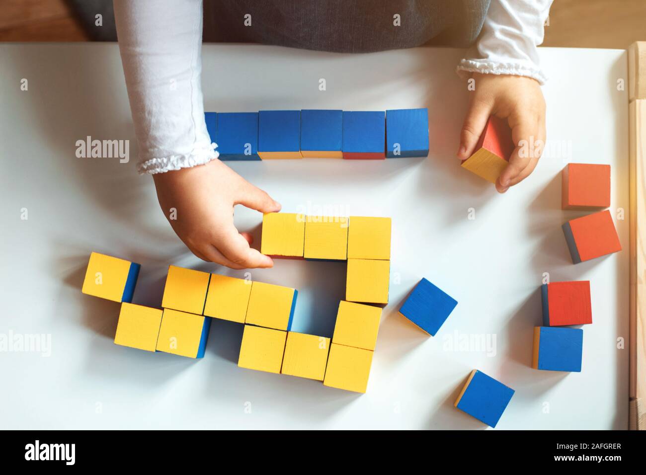 Little girl playing with colorful wooden bricks at home. She builds ...