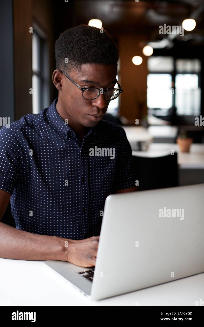 Young black male creative sitting at a desk in an open plan office ...
