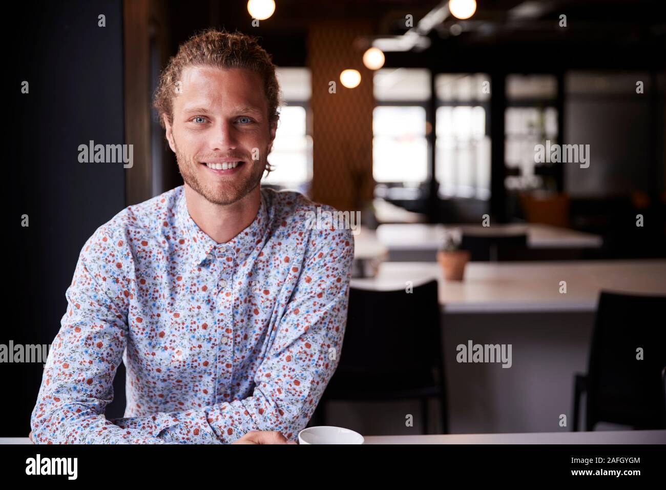 Millennial white male creative sitting at a desk in an open plan office ...