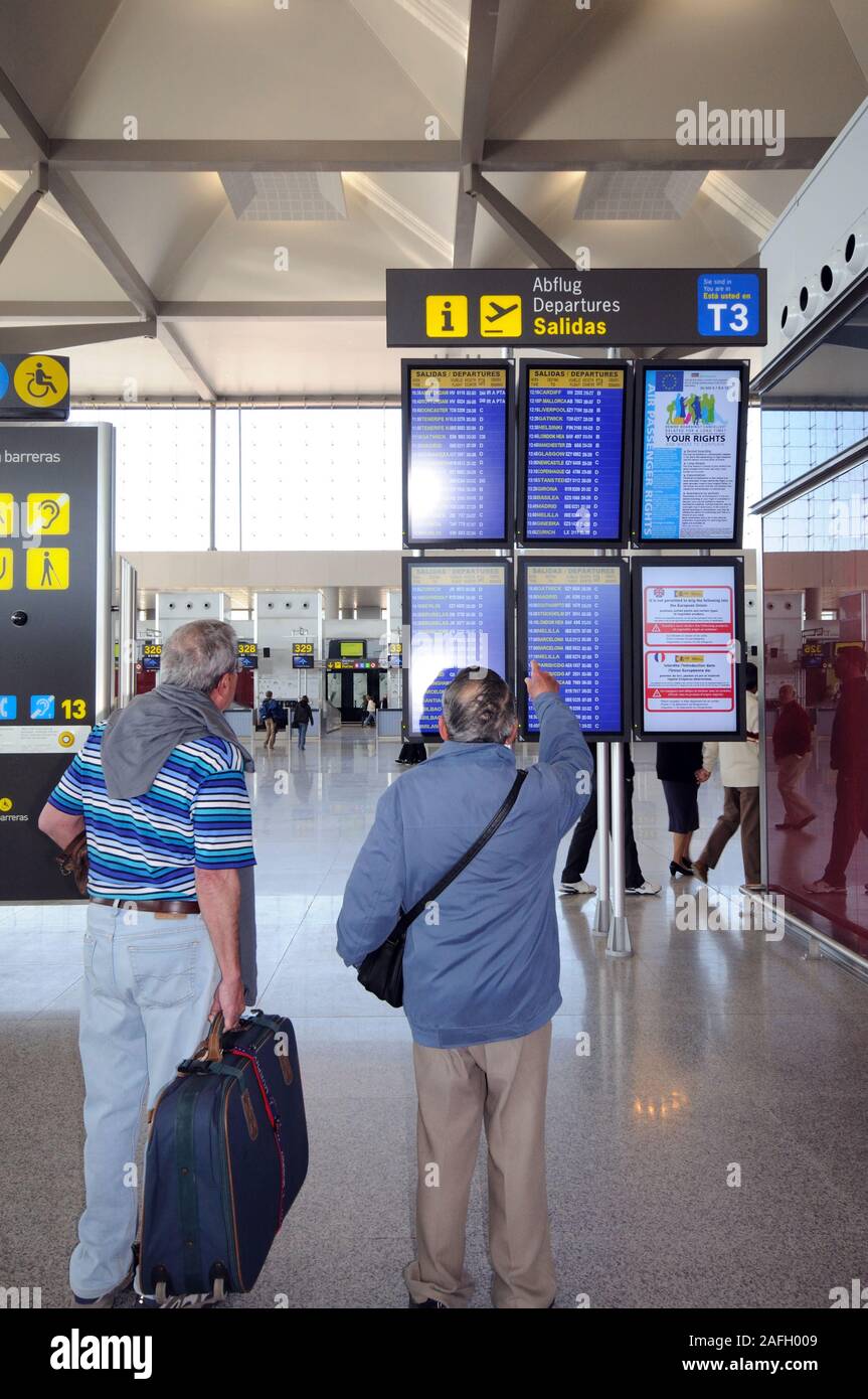Two people with suitcases standing reading the flight information ...