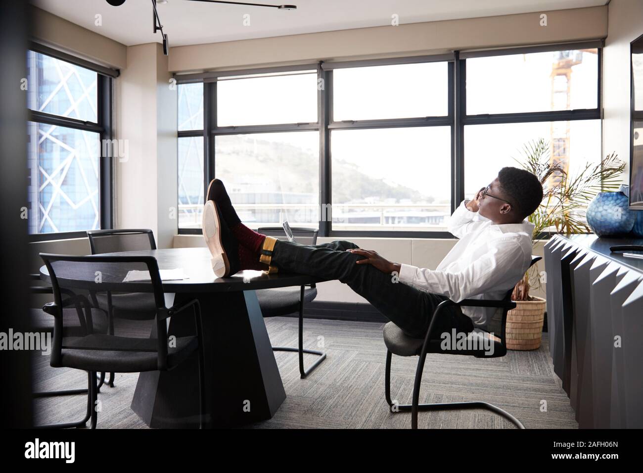 Millennial black businessman talking on the phone sitting with feet up ...