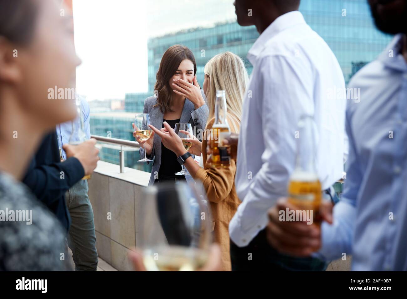 Office colleagues socialising with drinks on a balcony in the city ...