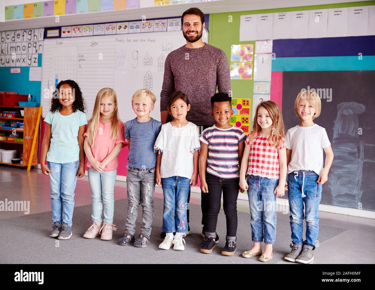Portrait Of Elementary School Pupils Standing In Classroom With Male ...