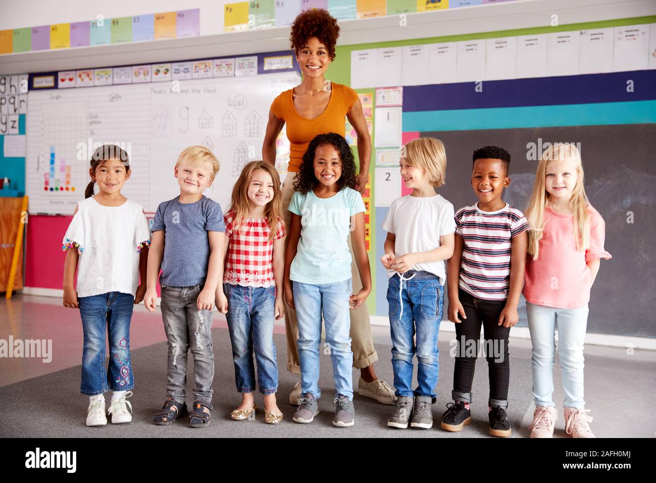 Portrait Of Elementary School Pupils Standing In Classroom With Female ...