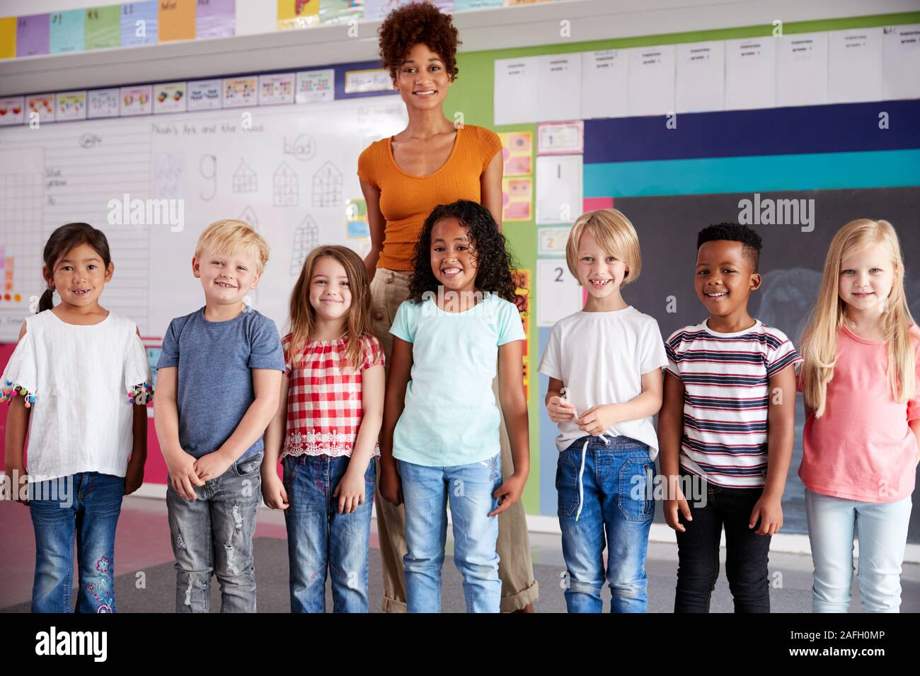 Portrait Of Elementary School Pupils Standing In Classroom With Female ...