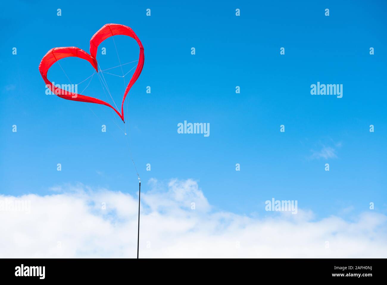 Single red heart shaped kites on a blue sky with white clouds with copy ...