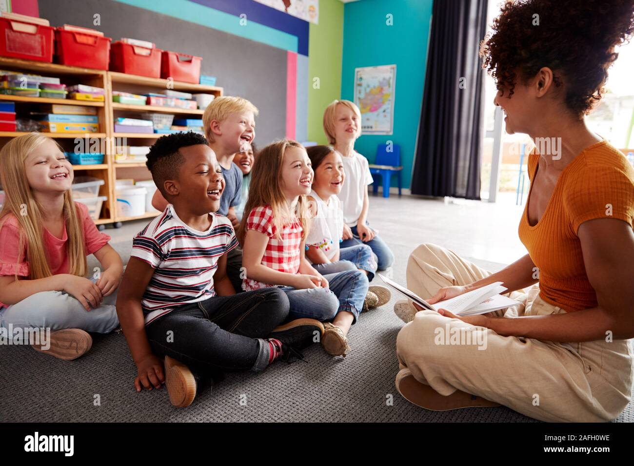 Group Of Elementary School Pupils Sitting On Floor Listening To Female ...