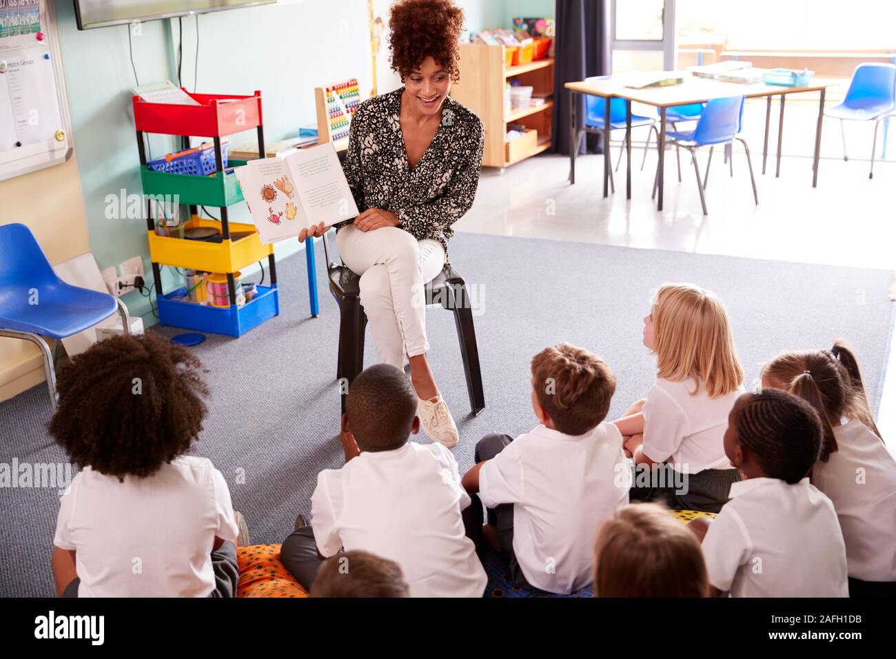 Female Teacher Reading Story To Group Of Elementary Pupils Wearing ...