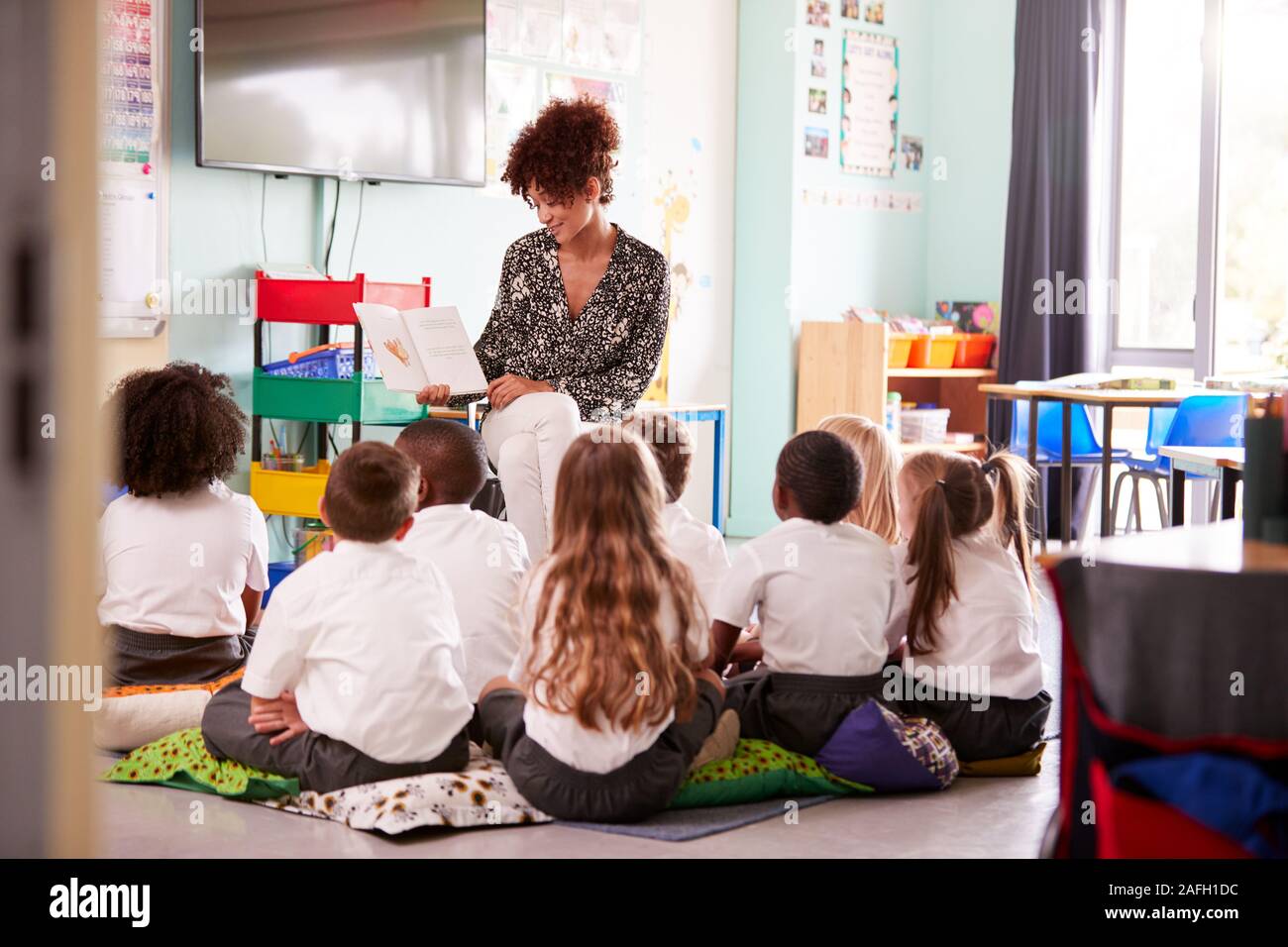 Female Teacher Reading Story To Group Of Elementary Pupils Wearing ...