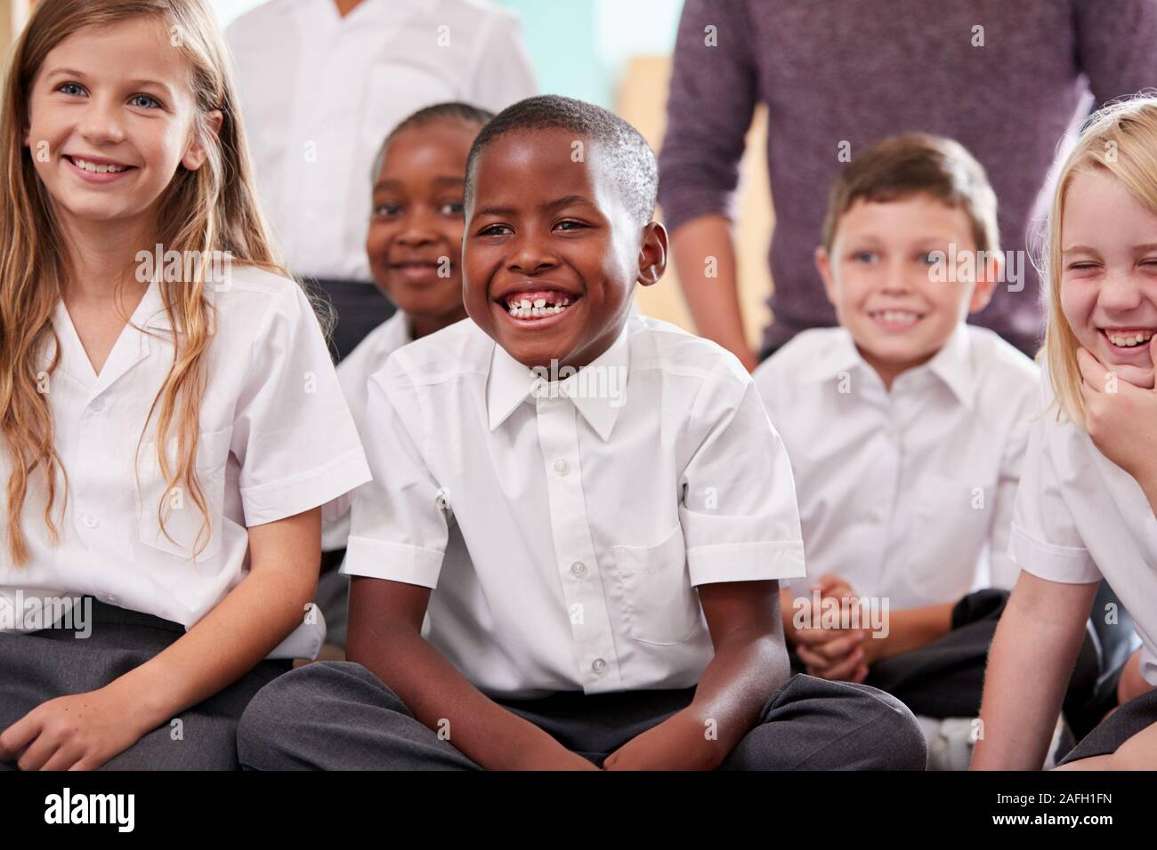 Group Of Elementary School Pupils Wearing Uniform Sitting On Floor ...