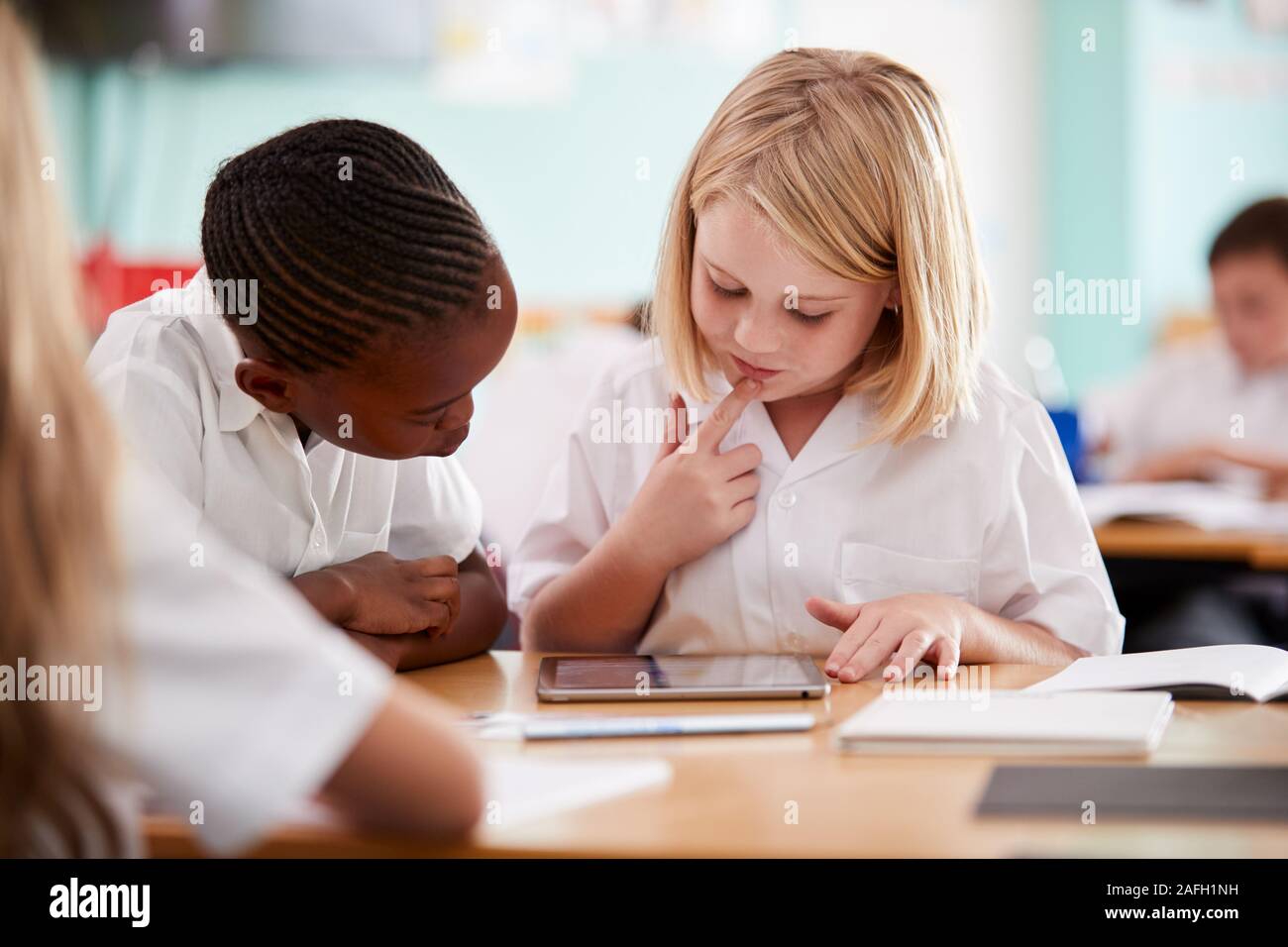Two Elementary School Pupils Wearing Uniform Using Digital Tablet At ...