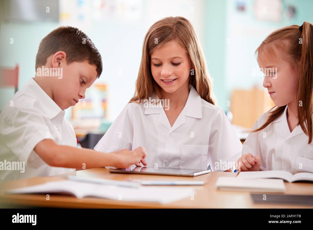 Three Elementary School Pupils Wearing Uniform Using Digital Tablet At ...