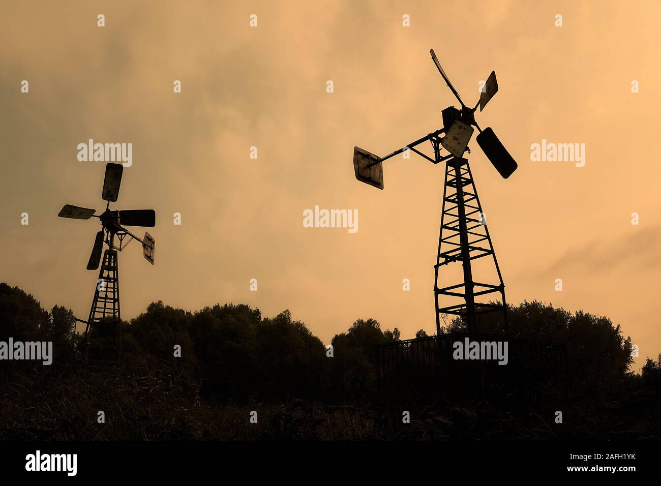 Two iron windmills and the silhouettes of trees under the yellow sky ...