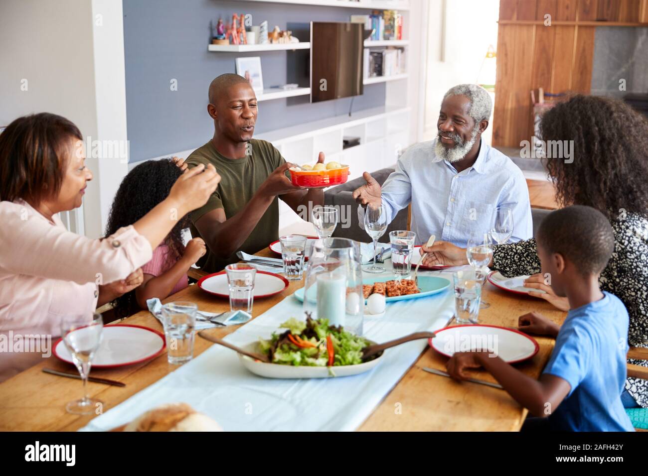 Multi-Generation Family Sitting Around Table At Home Enjoying Meal ...