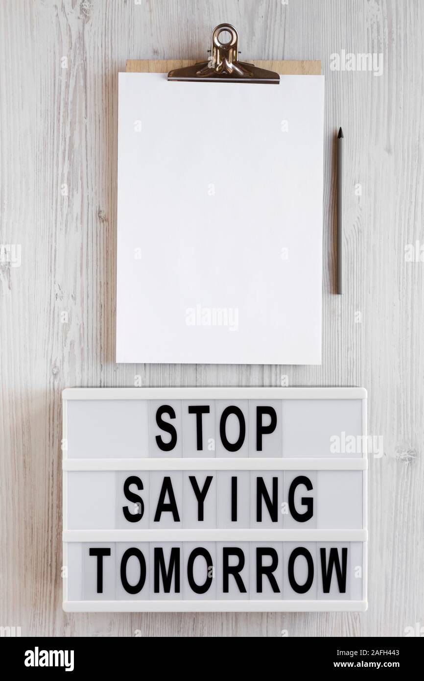 'Stop saying tomorrow' words on a lightbox, clipboard with blank sheet ...