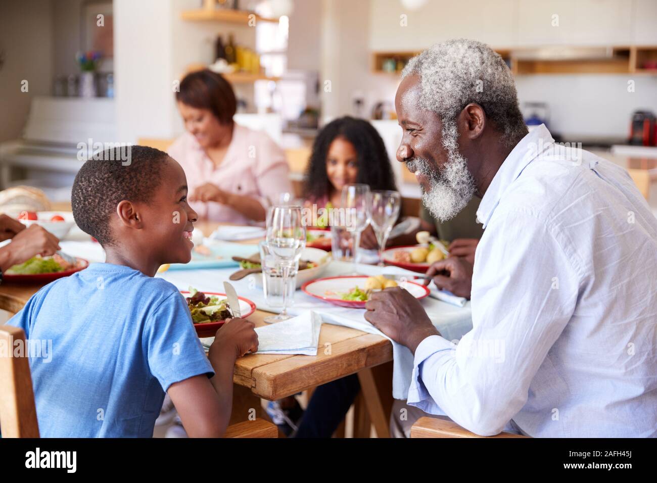 Multi-Generation Family Sitting Around Table At Home Enjoying Meal ...