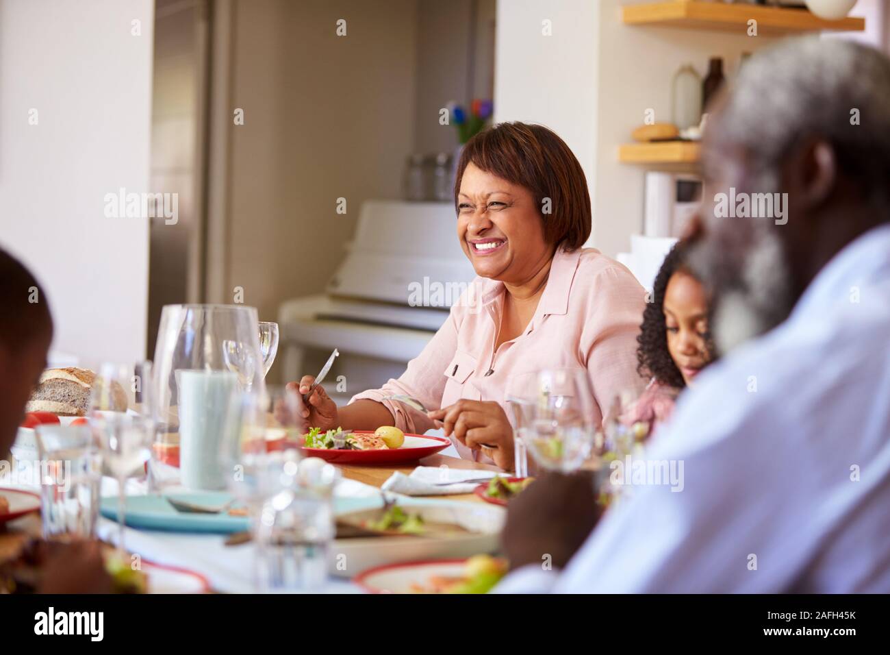 Multi-Generation Family Sitting Around Table At Home Enjoying Meal ...