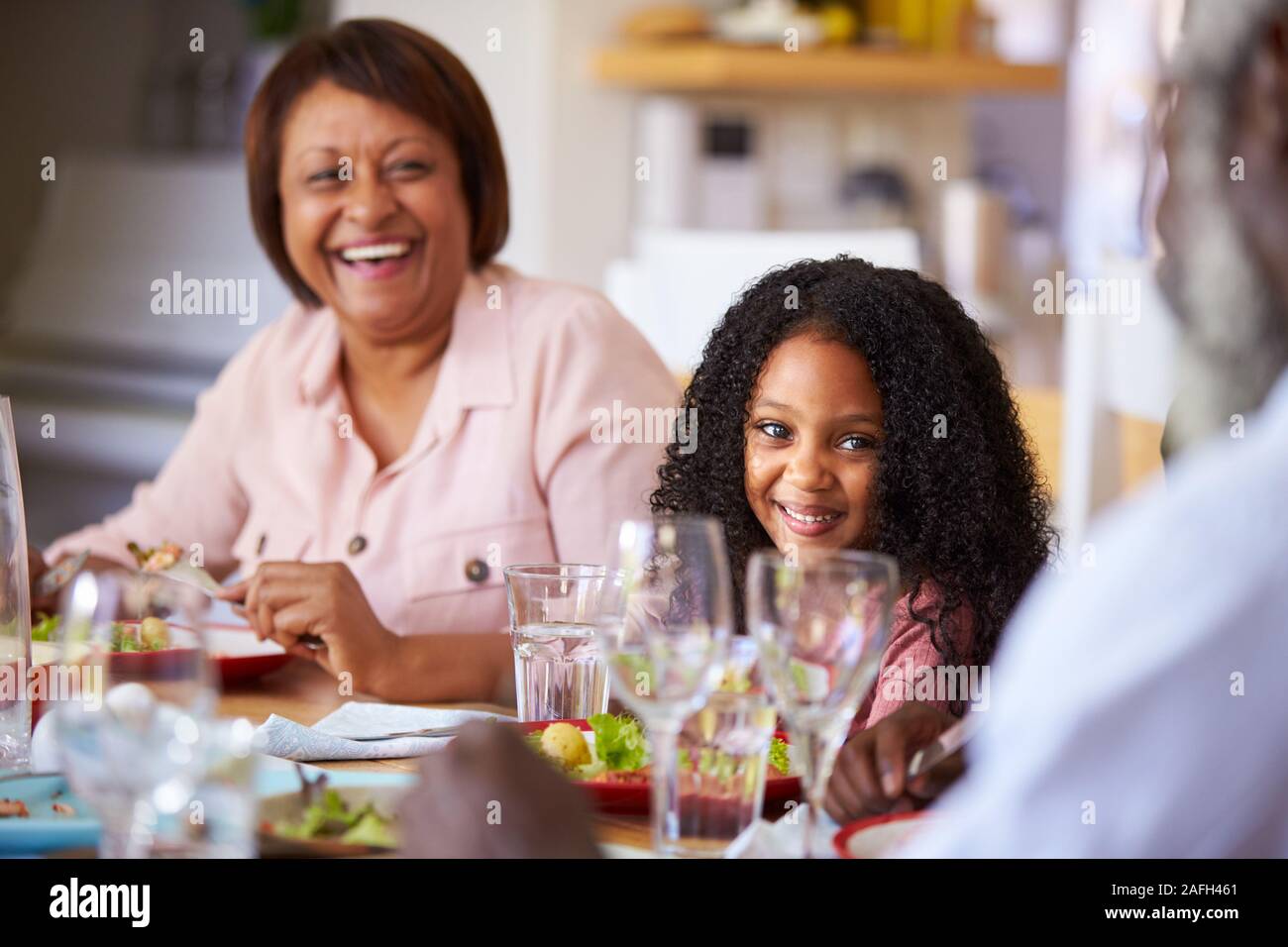 Multi-Generation Family Sitting Around Table At Home Enjoying Meal ...