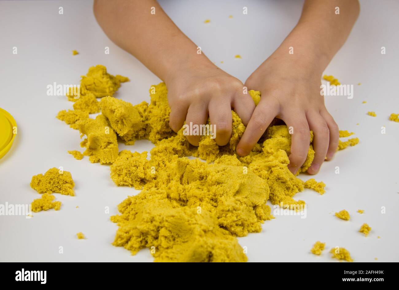 children's hands play yellow kinetic sand on a white table. Antistress ...