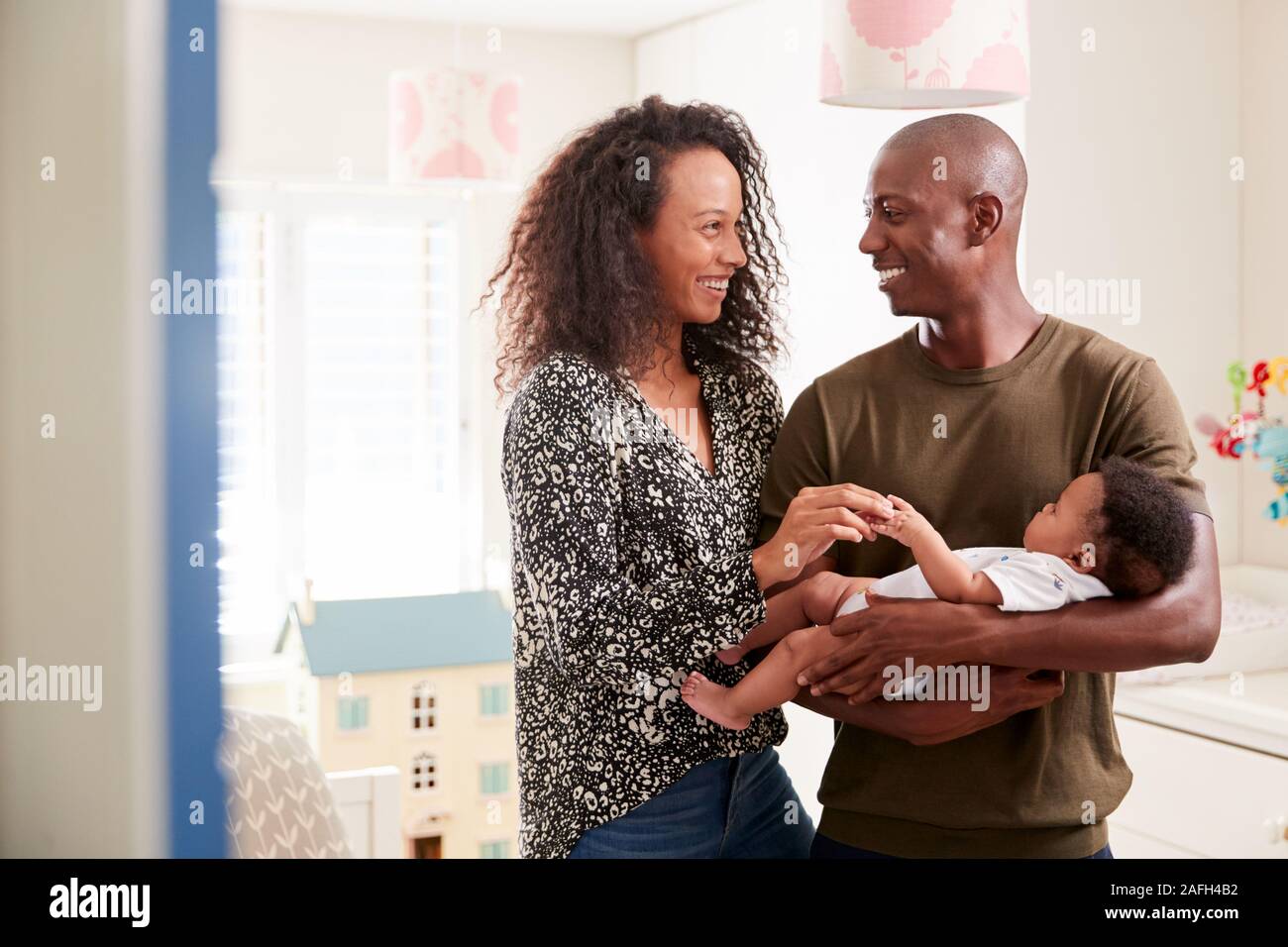 Loving Parents Standing In Nursery Cuddling Baby Son At Home Stock ...