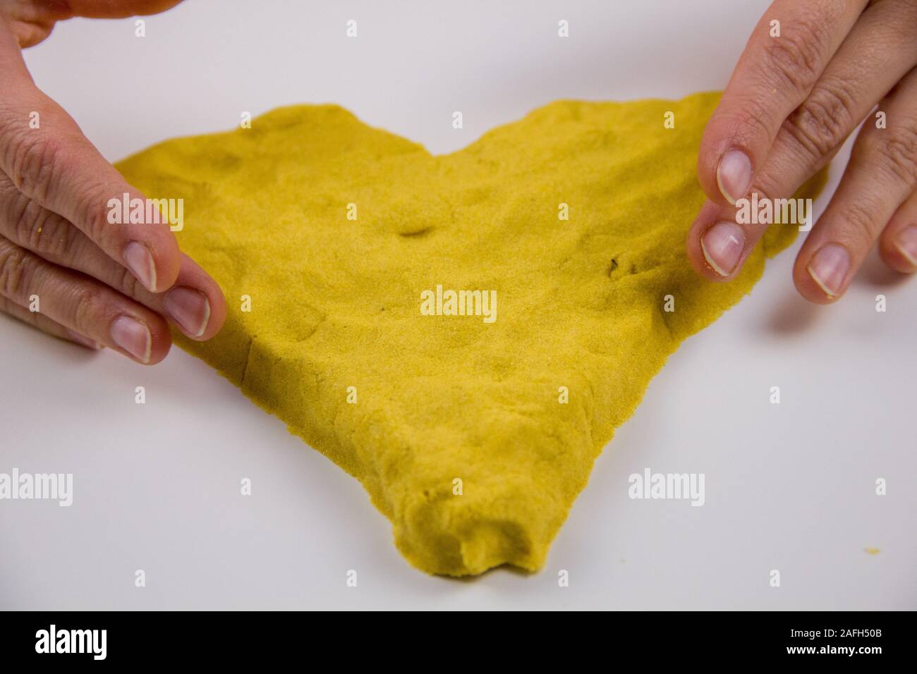 female hands mold yellow kinetic sand in the form of a heart on a white ...