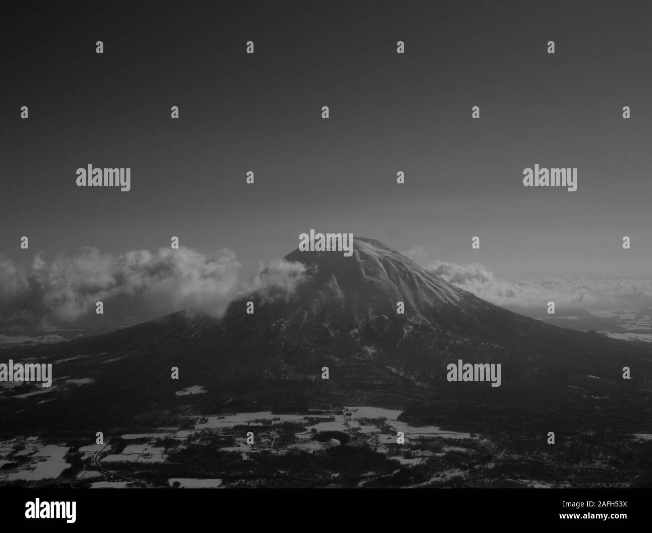 Greyscale scenery of a mountain blending in with the fluffy clouds ...