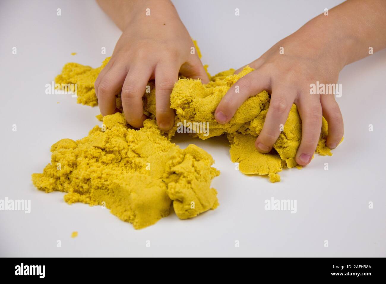children's hands play yellow kinetic sand on a white table. Antistress ...