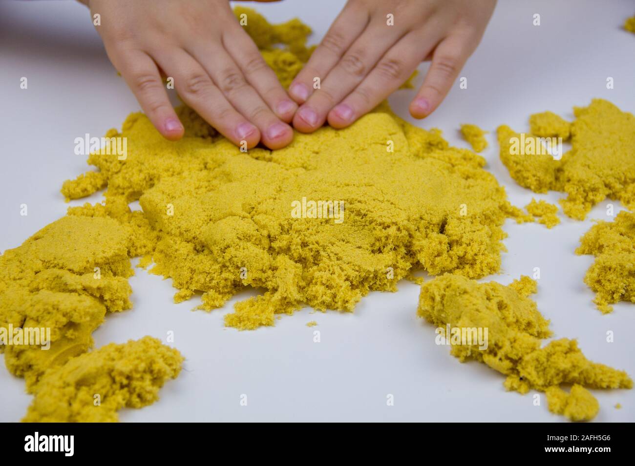 children's hands play yellow kinetic sand on a white table. Antistress ...