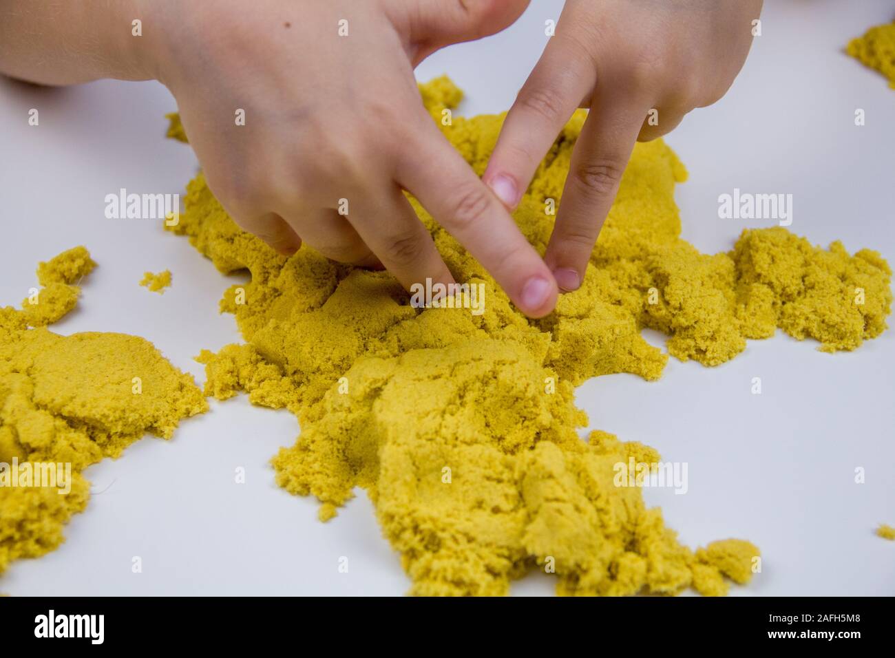 children's hands play yellow kinetic sand on a white table. Antistress ...