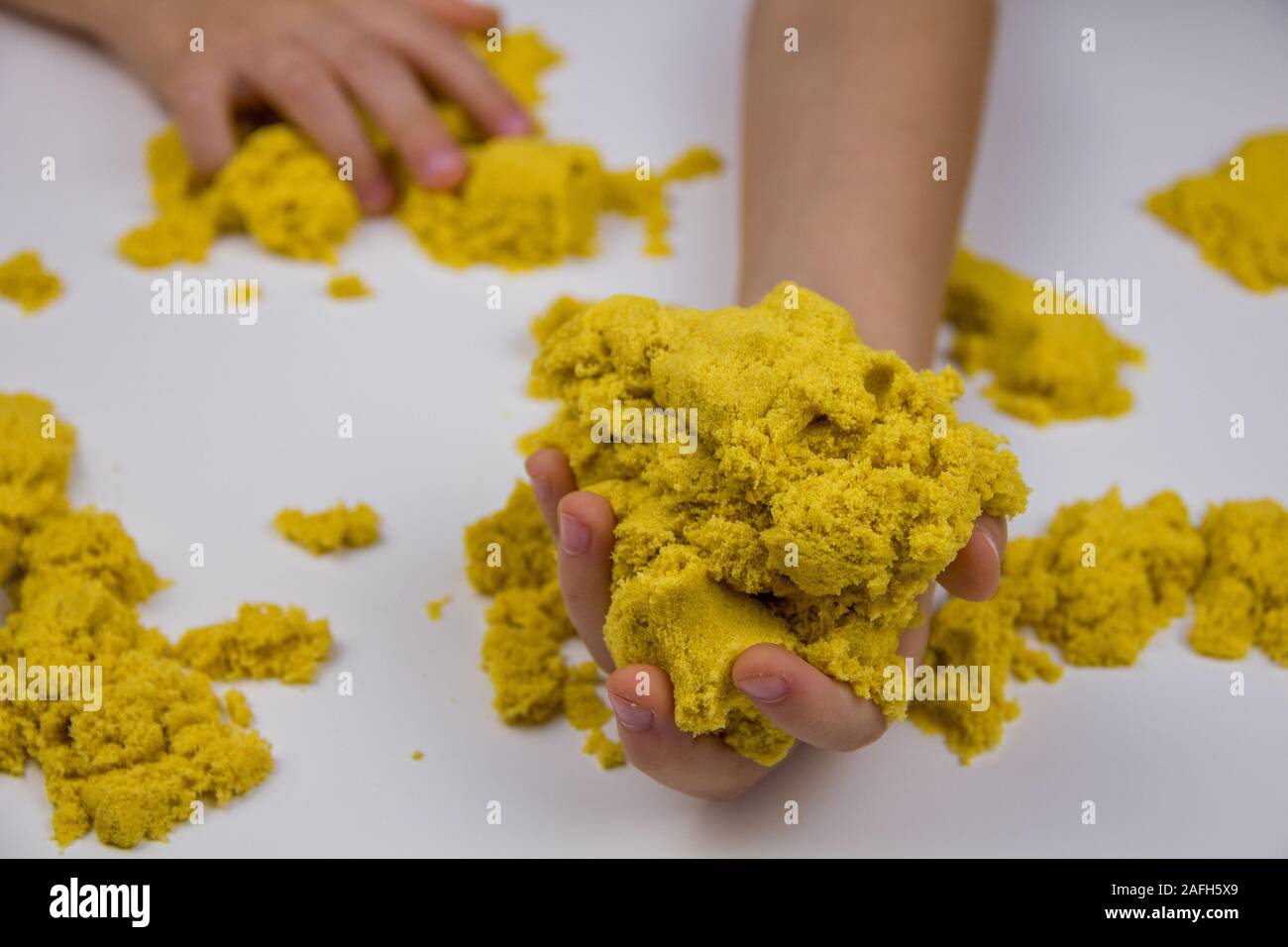 children's hands play yellow kinetic sand on a white table. Antistress ...