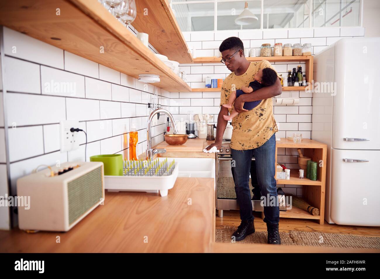 Multi-Tasking Father Holds Sleeping Baby Son And Cleans In Kitchen ...