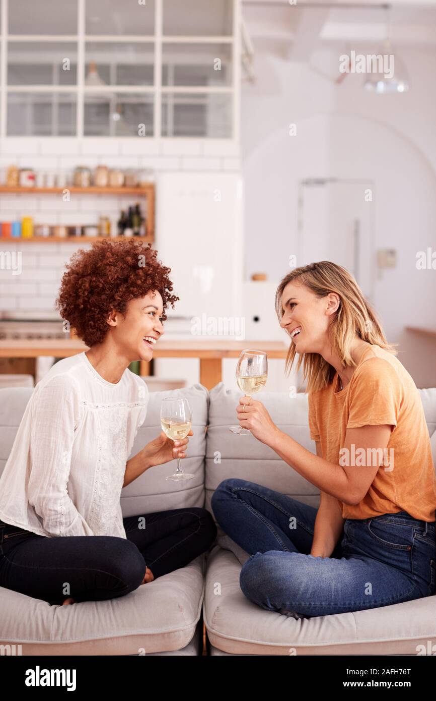 Two Female Friends Relaxing On Sofa At Home With Glass Of Wine Talking ...