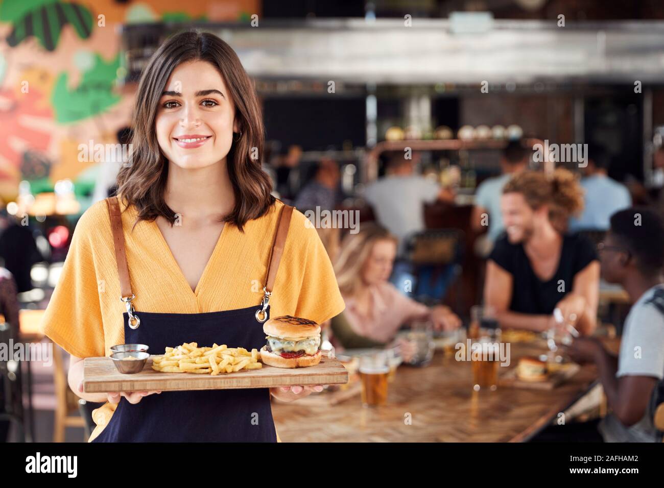Portrait Of Waitress Serving Food To Customers In Busy Bar Restaurant ...