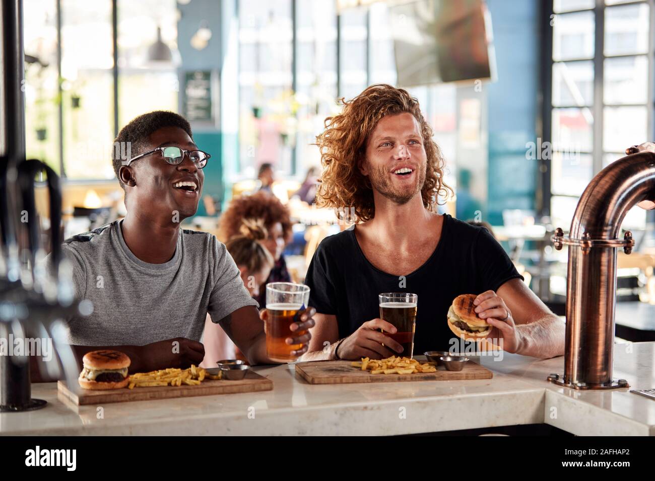 Two Male Friends Eating Food And Drinking Beer In Sports Bar Stock ...